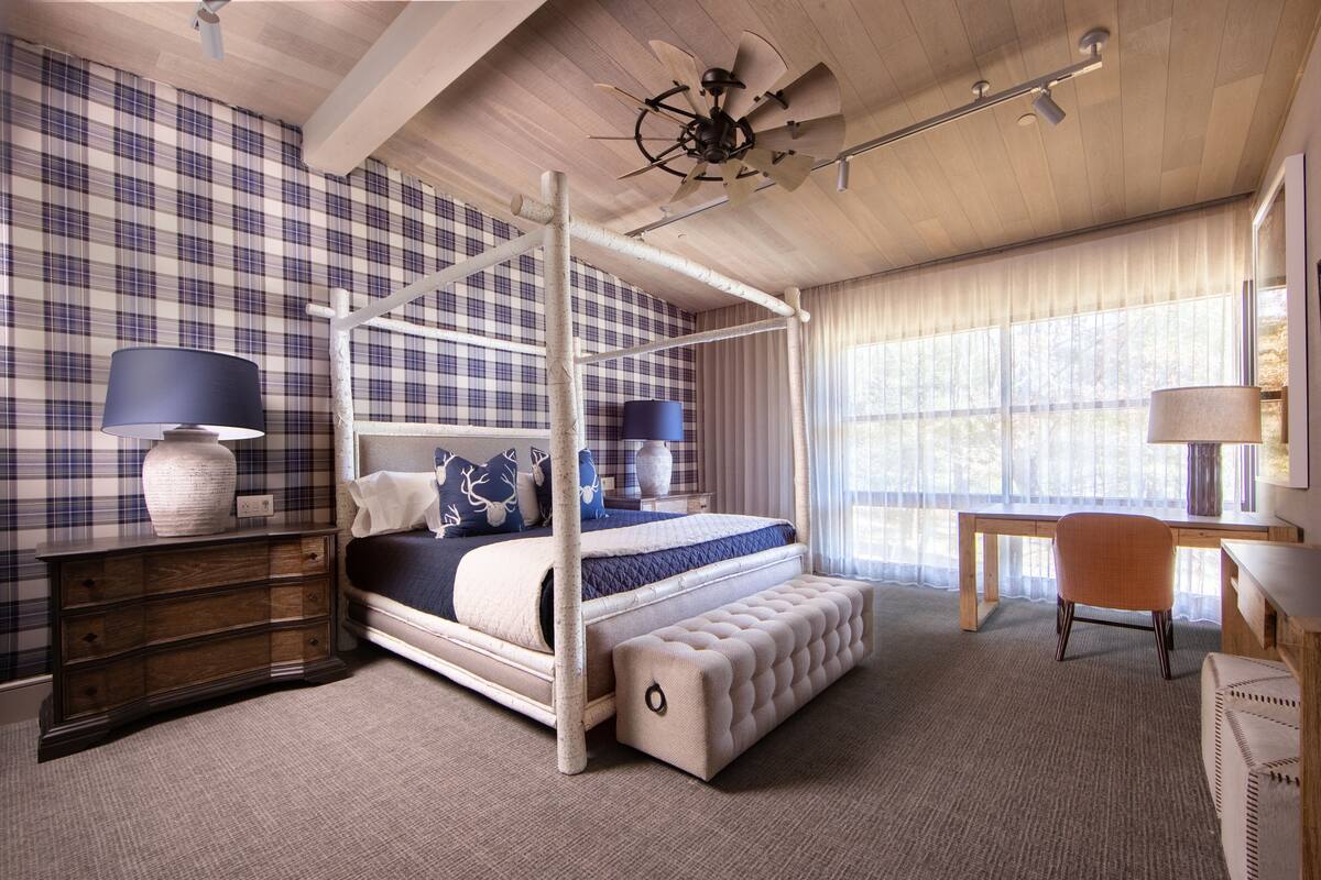 Uma cama de dossel com cortina, uma escrivaninha com cadeira e uma janela grande com cortinas leves.