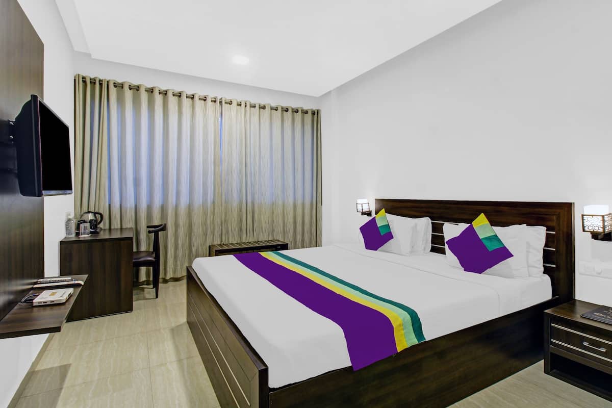 Quarto de hotel com cama, mesas de cabeceira, televisão e janela com cortinas.