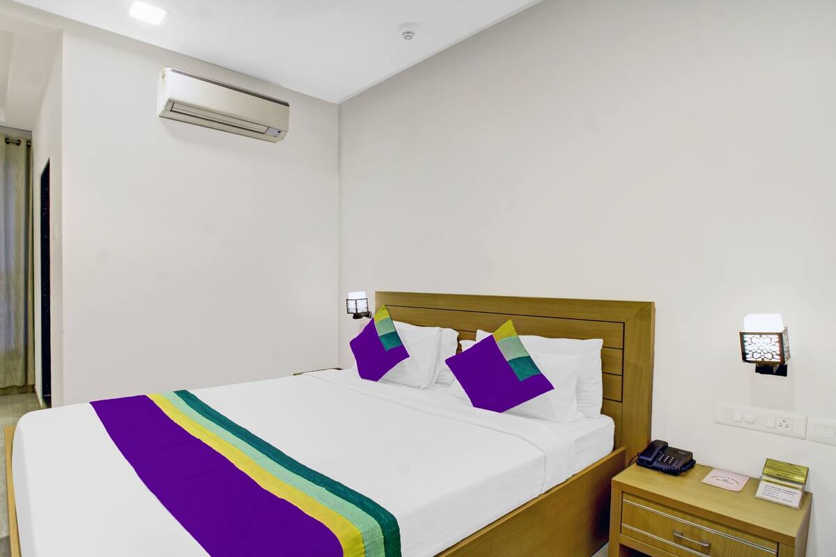 Quarto de hotel com cama, mesa de cabeceira, abajur e ar condicionado.