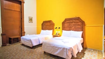 Quarto com duas camas, cabeceiras de madeira, um banco e ladrilhos estampados.