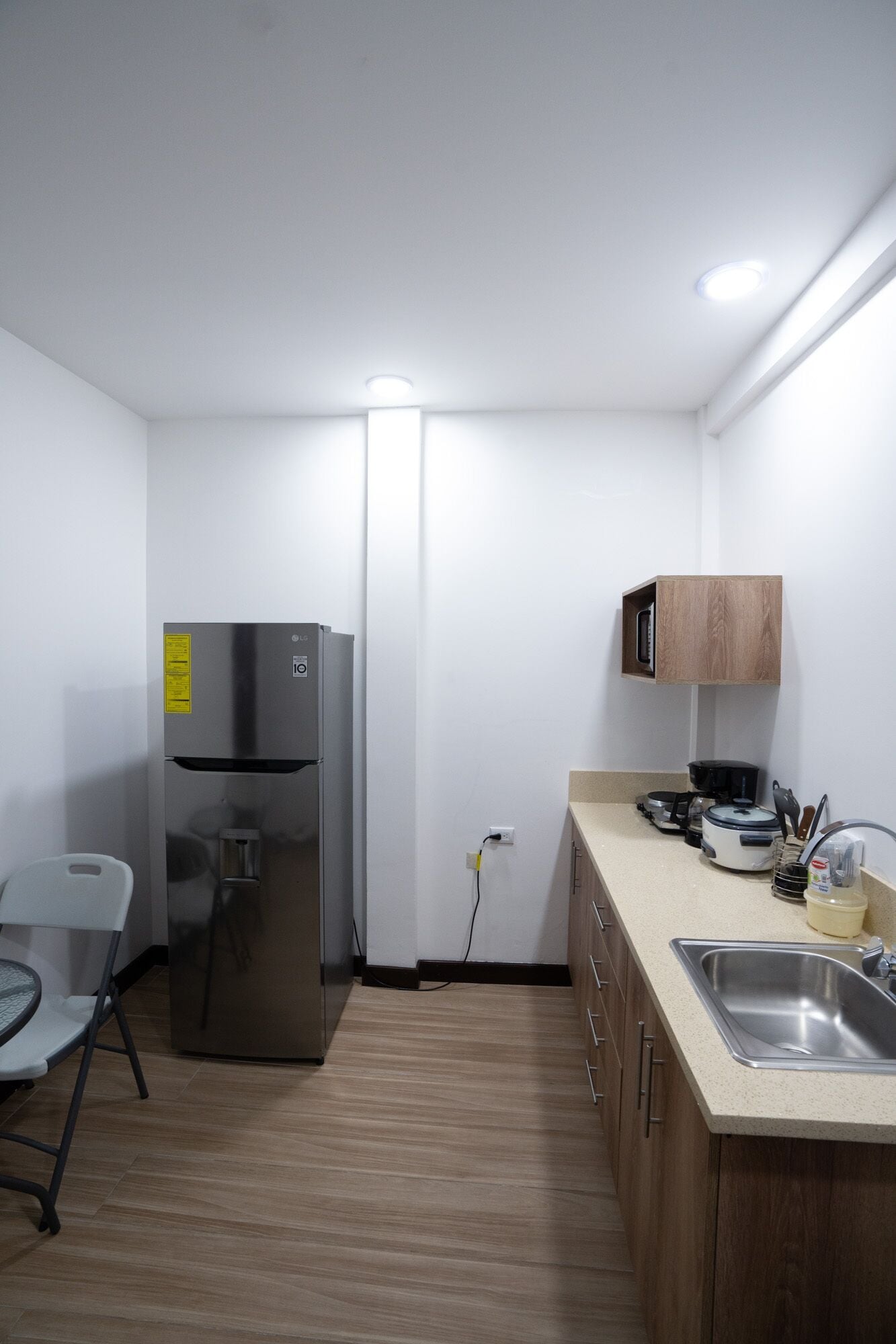 Uma cozinha compacta com frigorífico em aço inoxidável, um armário de madeira, uma pia e um espaço de refeições com uma cadeira.