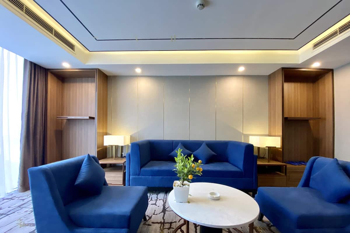 Quarto de hotel moderno com um sofá azul, uma mesa de centro redonda e uma planta em vaso.