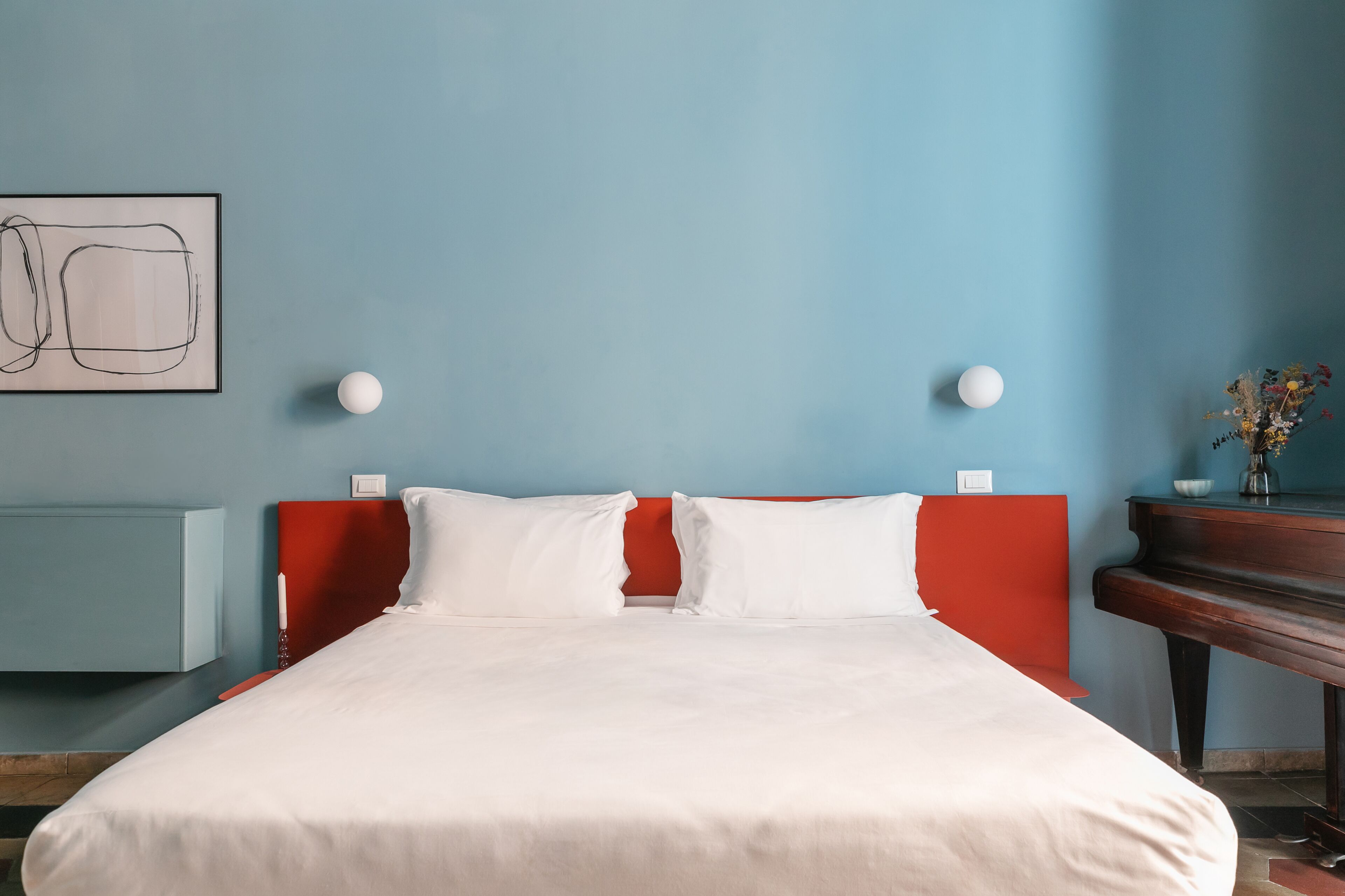 Uma cama bem arrumada com lençóis brancos, uma cabeceira vermelha e duas luminárias de cabeceira.