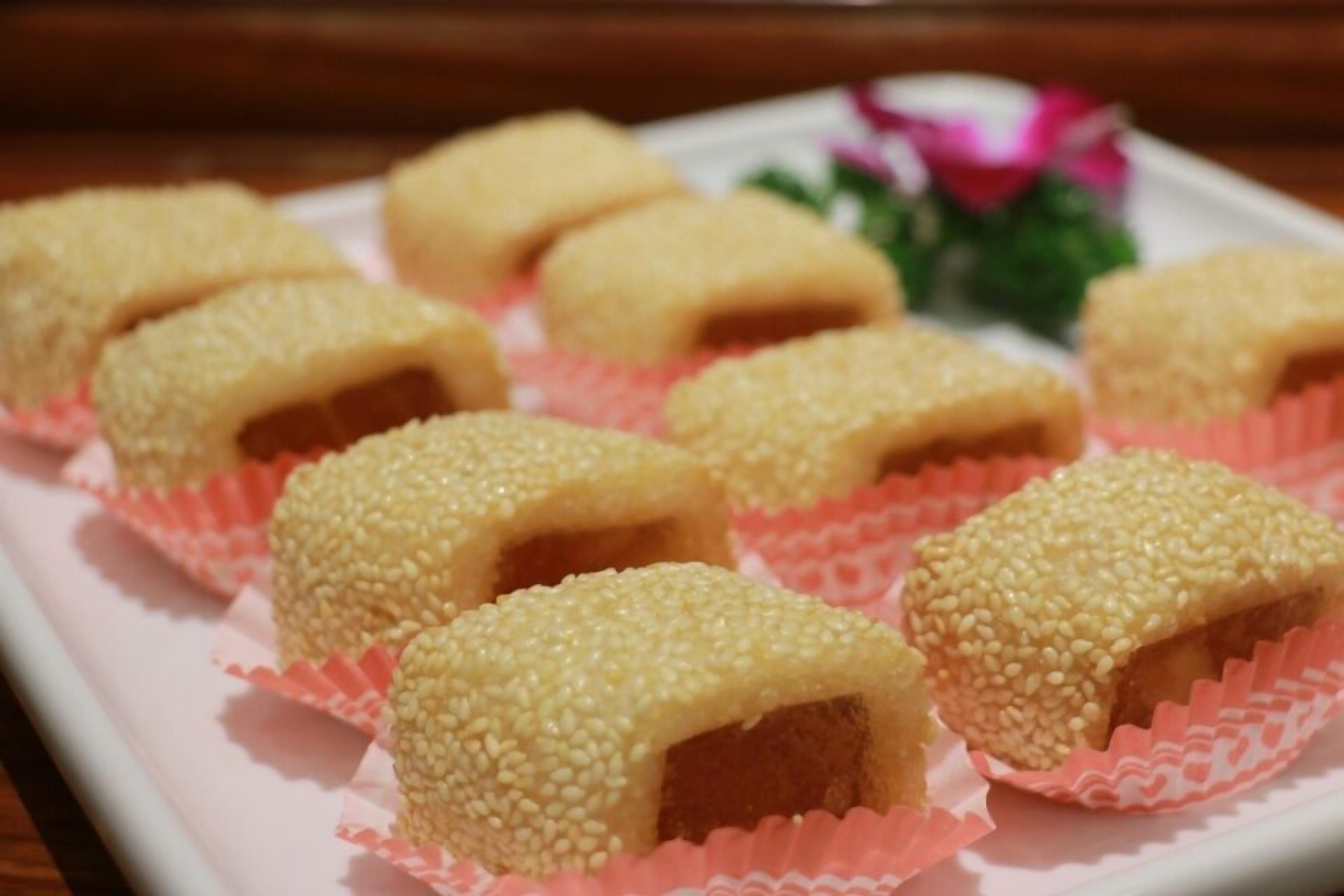 Uma bandeja de doces cobertos de sementes de sésamo em copinhos de papel rosa.