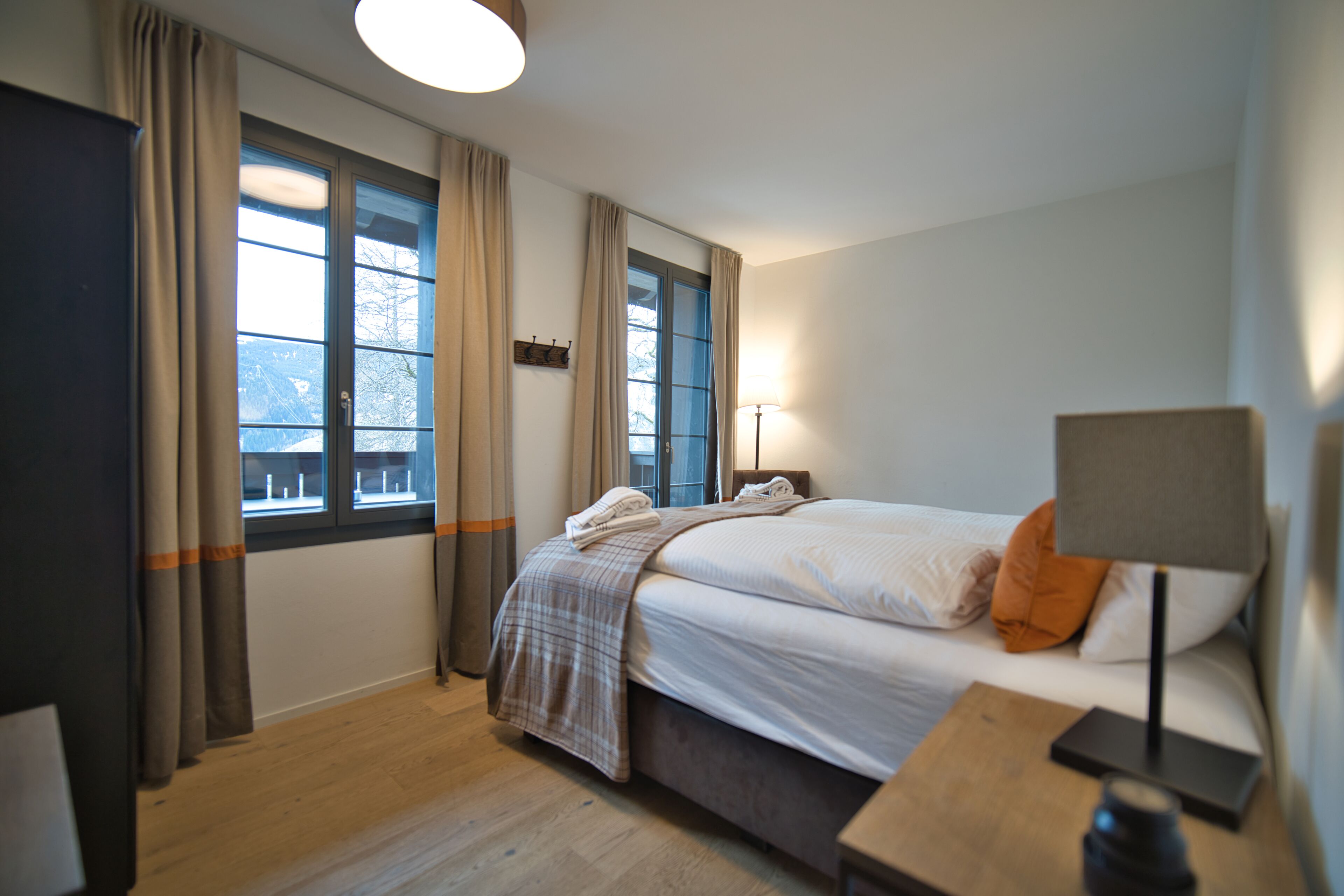 Quarto de hotel com cama, mesa de cabeceira, abajur e cortinas.