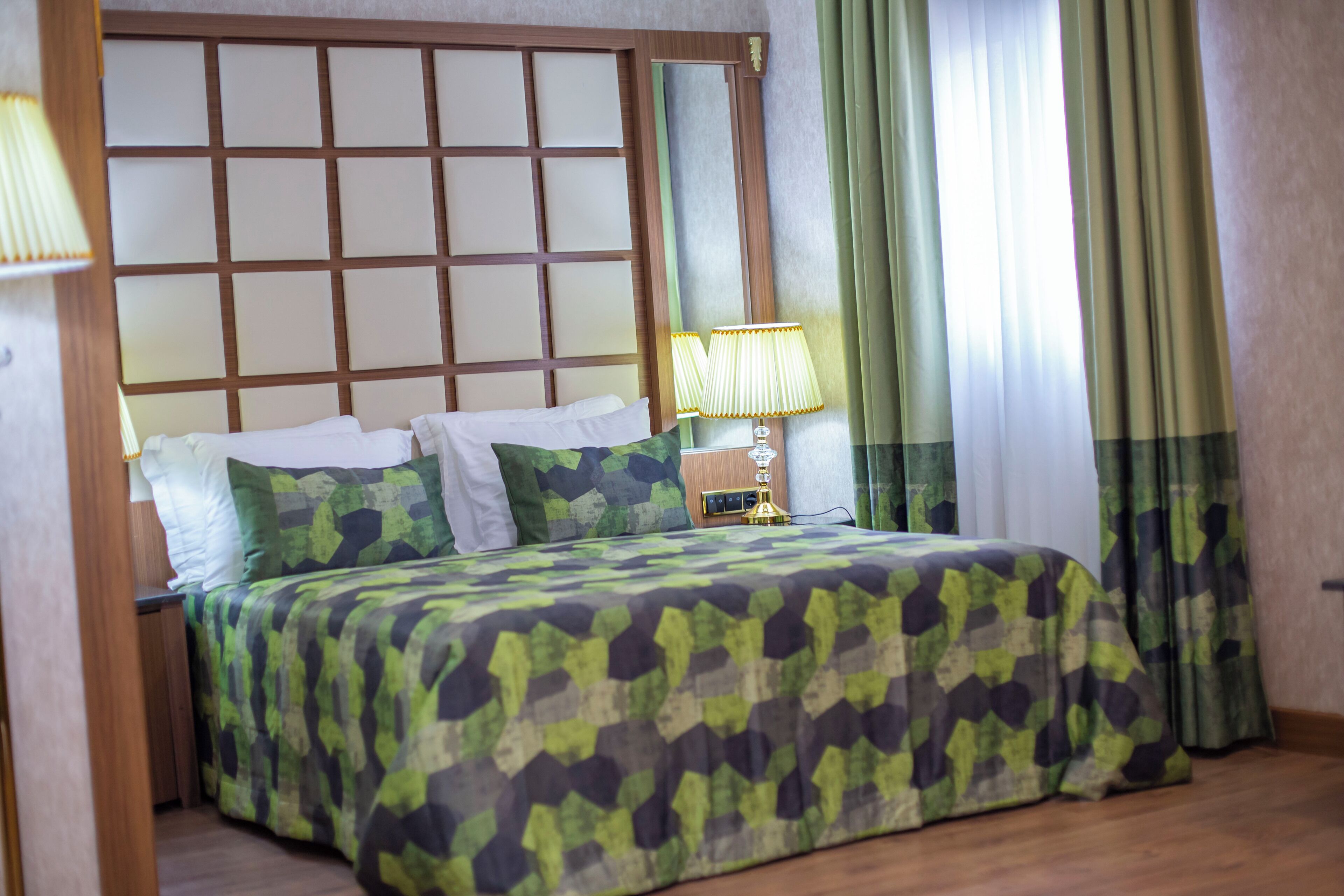 Uma cama bem arrumada com colcha estampada, abajur e cortinas.