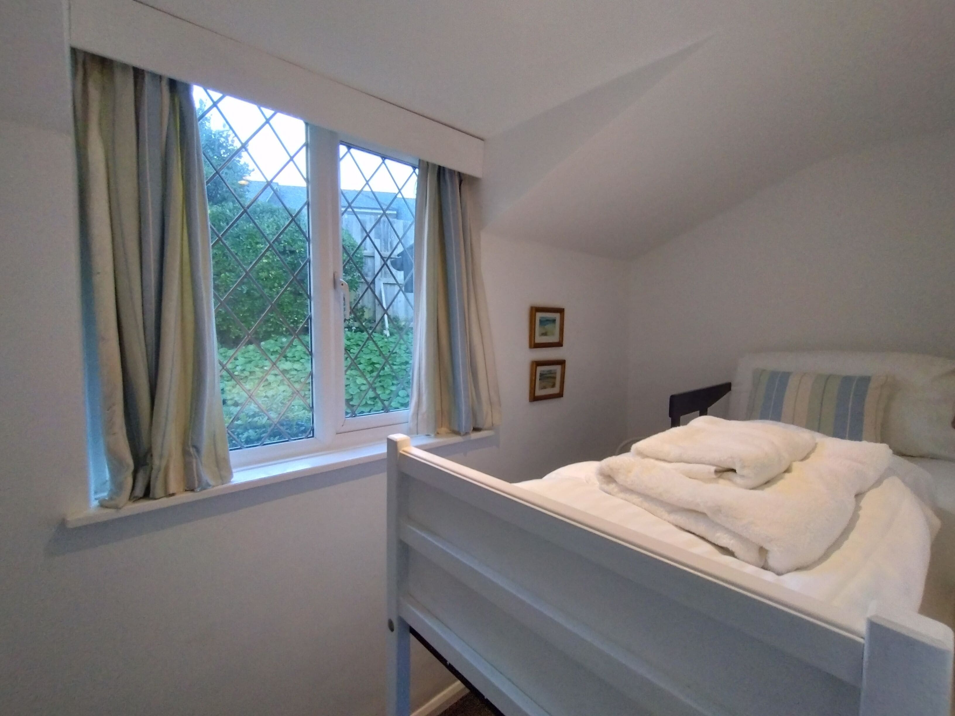 Quarto com cama, janela com cortinas e duas imagens emolduradas na parede.