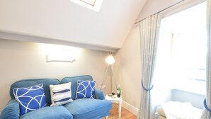 Uma sala de estar moderna com um sofá azul, uma pequena mesa lateral branca e um candeeiro suspenso.