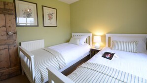 Quarto de hotel com duas camas, uma porta de madeira e dois quadros florais na parede.