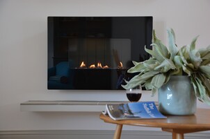 Uma sala de estar moderna com televisão de tela plana na parede, uma planta em vaso sobre uma mesinha e uma revista.