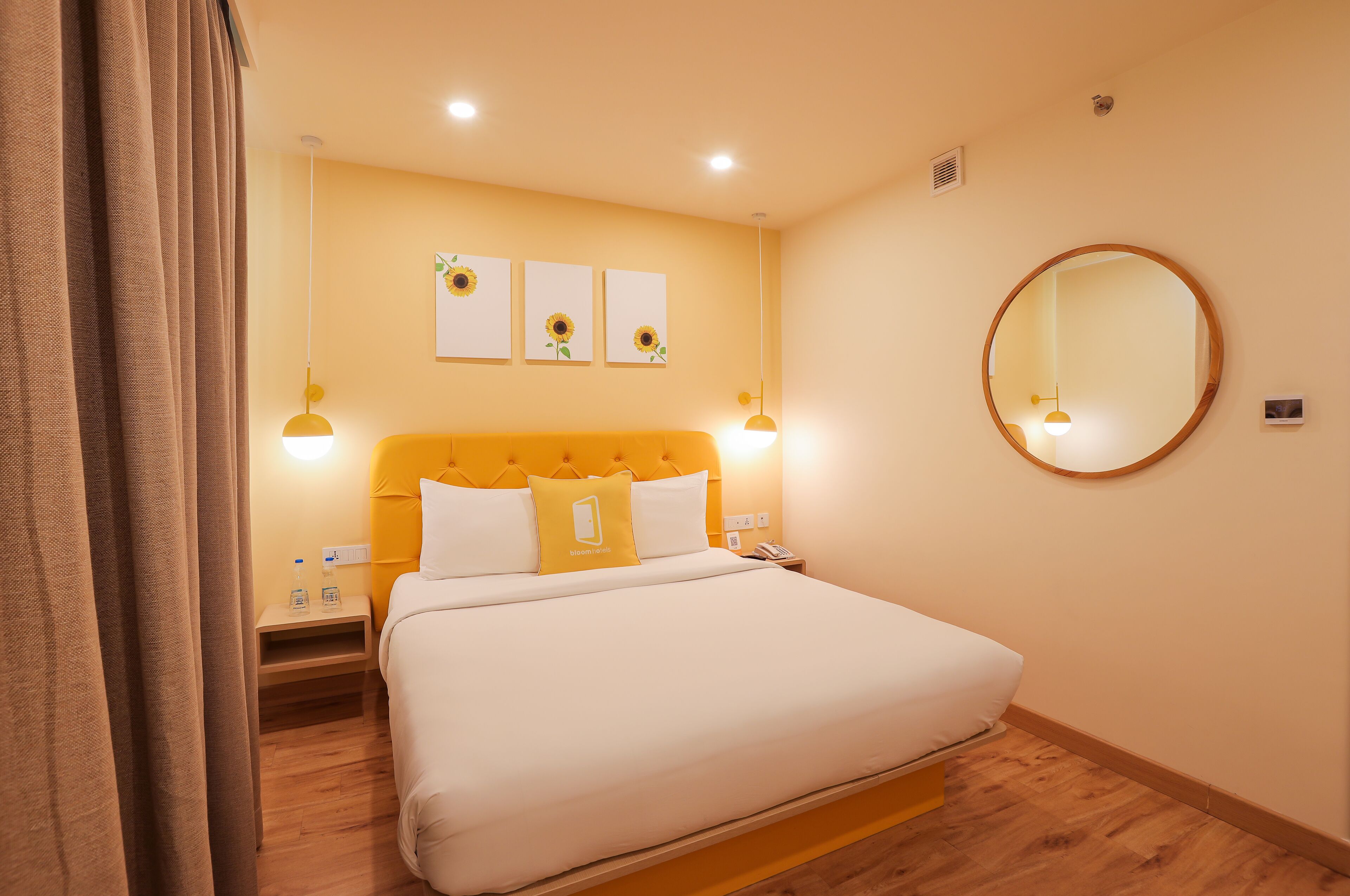 Quarto de hotel com cama, mesas de cabeceira, espelho e quadros nas paredes.