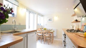 Cozinha moderna com bancadas de madeira, lava-louças embutida, espaço de refeições com mesa e cadeiras, e janela que proporciona luz natural.