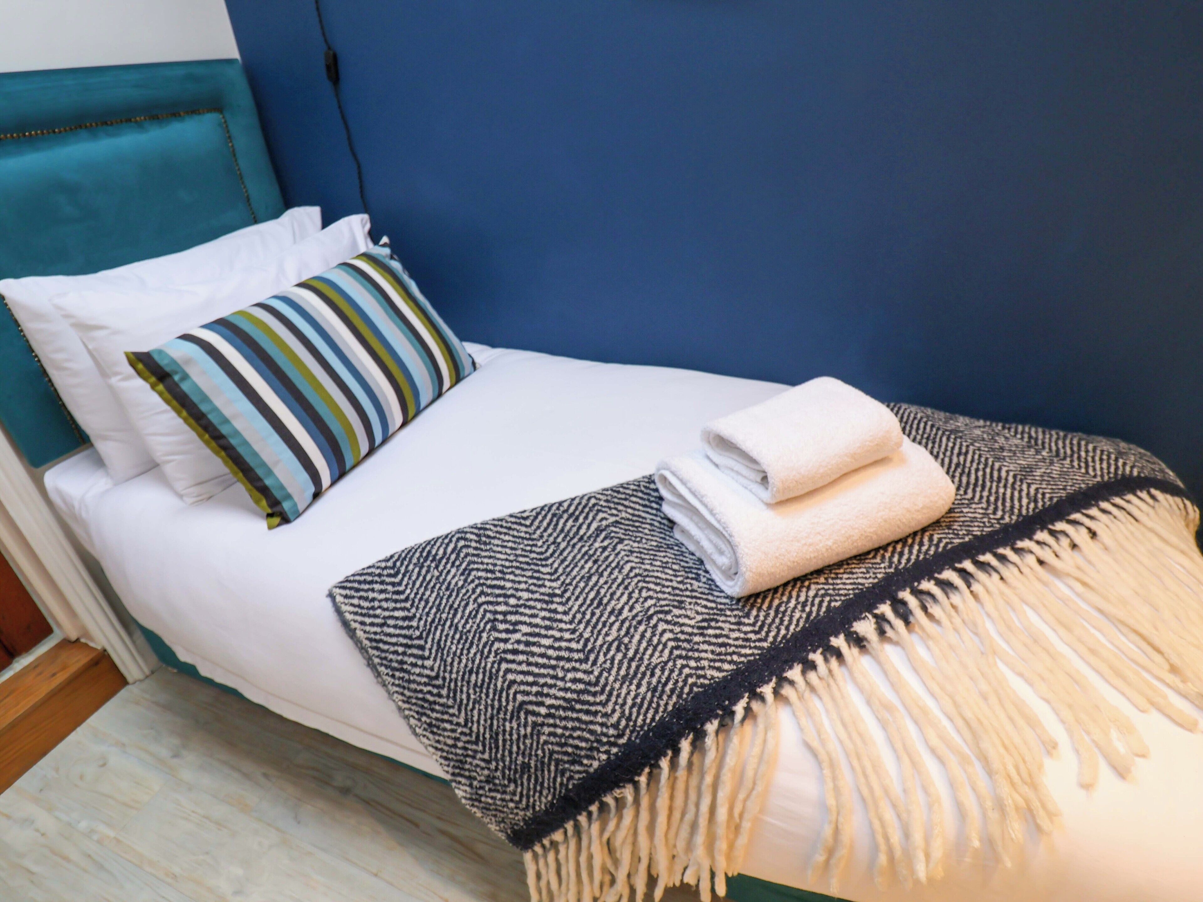 Cama bem arrumada com travesseiro listrado, toalha branca dobrada e manta estampada.