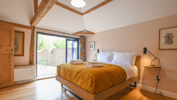 Quarto com cama de madeira, radiador branco, janela com cortinas e uma porta.