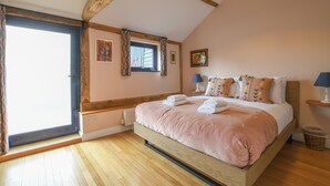 Um quarto com uma cama grande, vigas de madeira, uma janela com cortinas e um radiador.