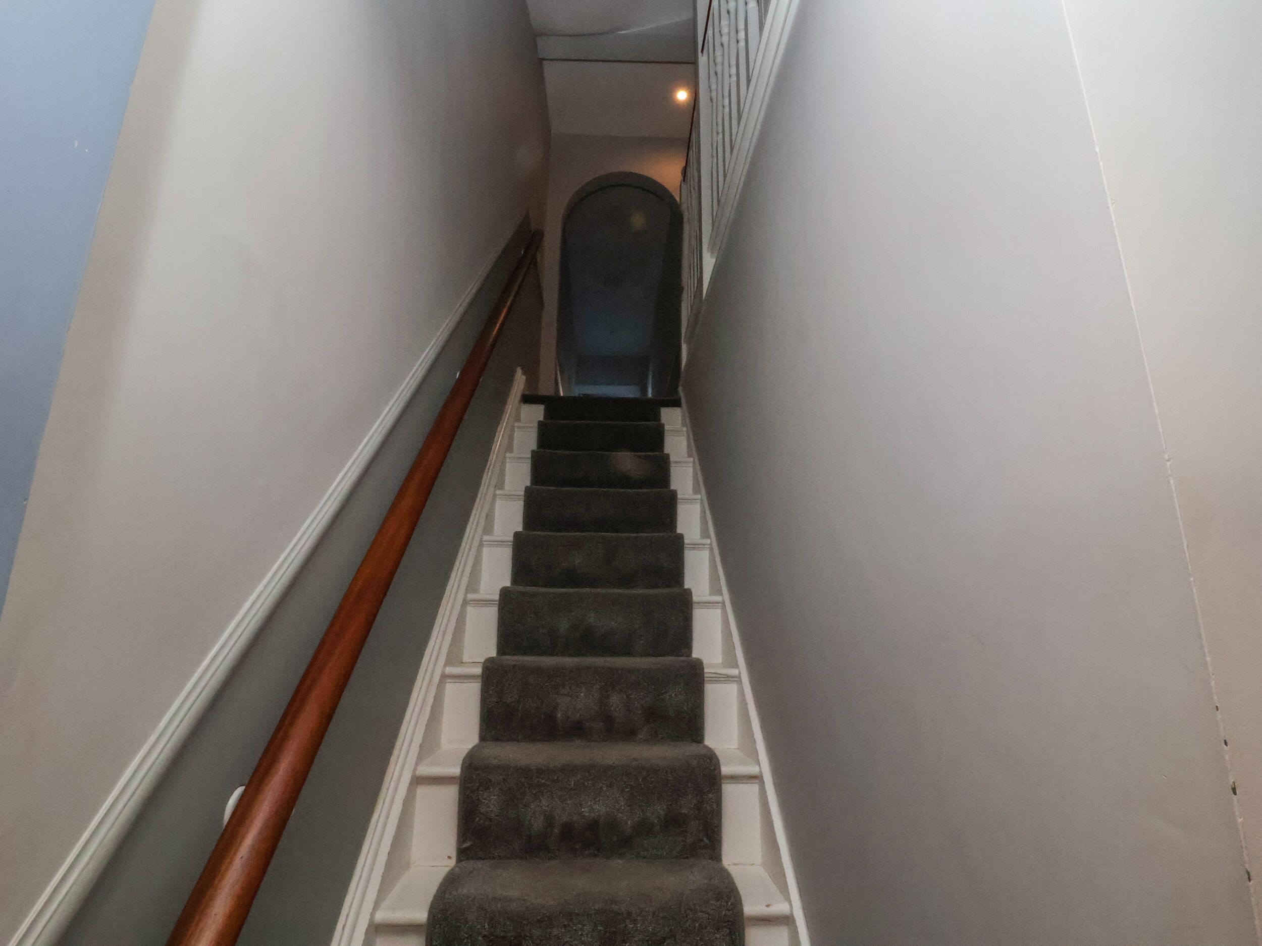 Uma escada com corrimão, degraus carpetados e paredes brancas.
