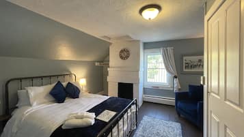 Quarto com cama, luminária de cabeceira, relógio e vista para o exterior através de uma janela.