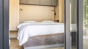 Quarto moderno com cama grande, cabeceira de madeira e parede estampada.