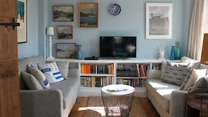 Uma sala de estar com sofá, mesa de centro e estante repleta de livros.