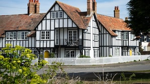 Um edifício tradicional em estilo Tudor, com estrutura de madeira branca e preta, várias chaminés e uma cerca de piquete branca.