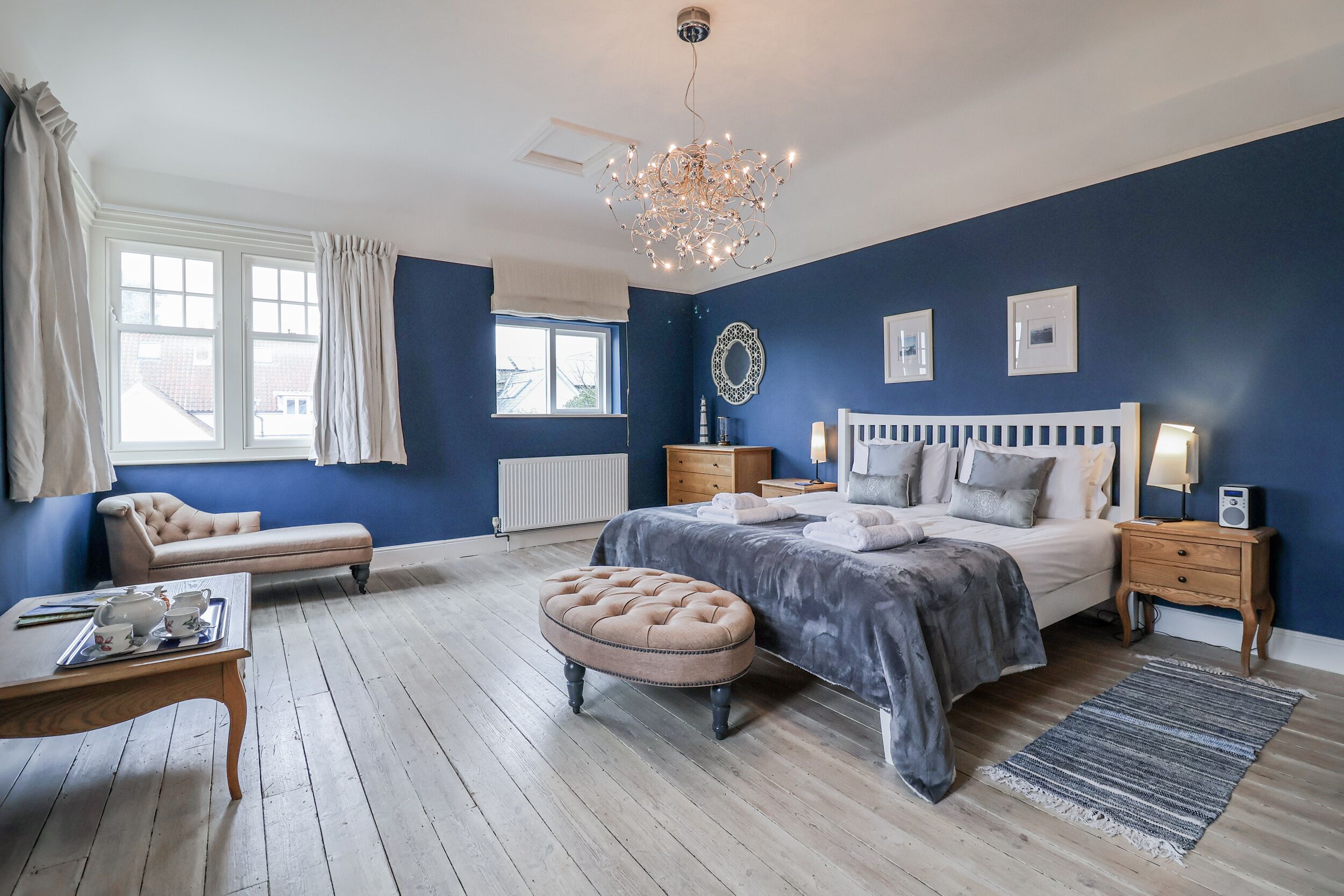 Quarto com cama, mesas de cabeceira, um banquinho, um candelabro e vista para o exterior.