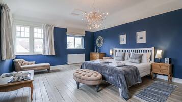 Quarto com cama, mesas de cabeceira, um banquinho, um candelabro e vista para o exterior.