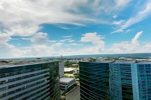 Um edifício alto com fachada de vidro moderna, céu claro com nuvens esparsas e vista distante de um horizonte urbano.