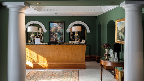 Uma área de recepção com um balcão de madeira, duas luminárias, um quadro e um vaso com flores.
