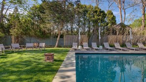 Um quintal com piscina, espreguiçadeiras e um vaso de pedra.