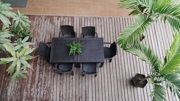 Uma área de refeições ao ar livre com mesa e cadeiras, rodeada por plantas em vasos.