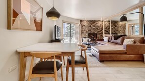 Uma sala de estar moderna com área de jantar, parede de pedra e janelas amplas.