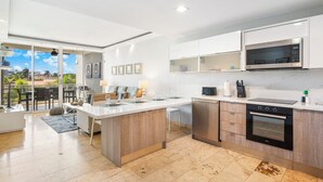 Cozinha moderna com ilha central, micro-ondas embutido, forno e uma grande janela com vista para uma varanda.
