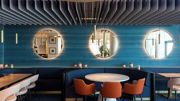 Um restaurante moderno com esquema de cores azul e branco, mesas redondas e cadeiras laranja, e um design de teto único.
