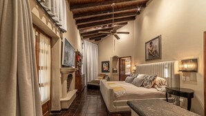 Um quarto com cama, escrivaninha, cadeira, lareira e ventoinha no teto.