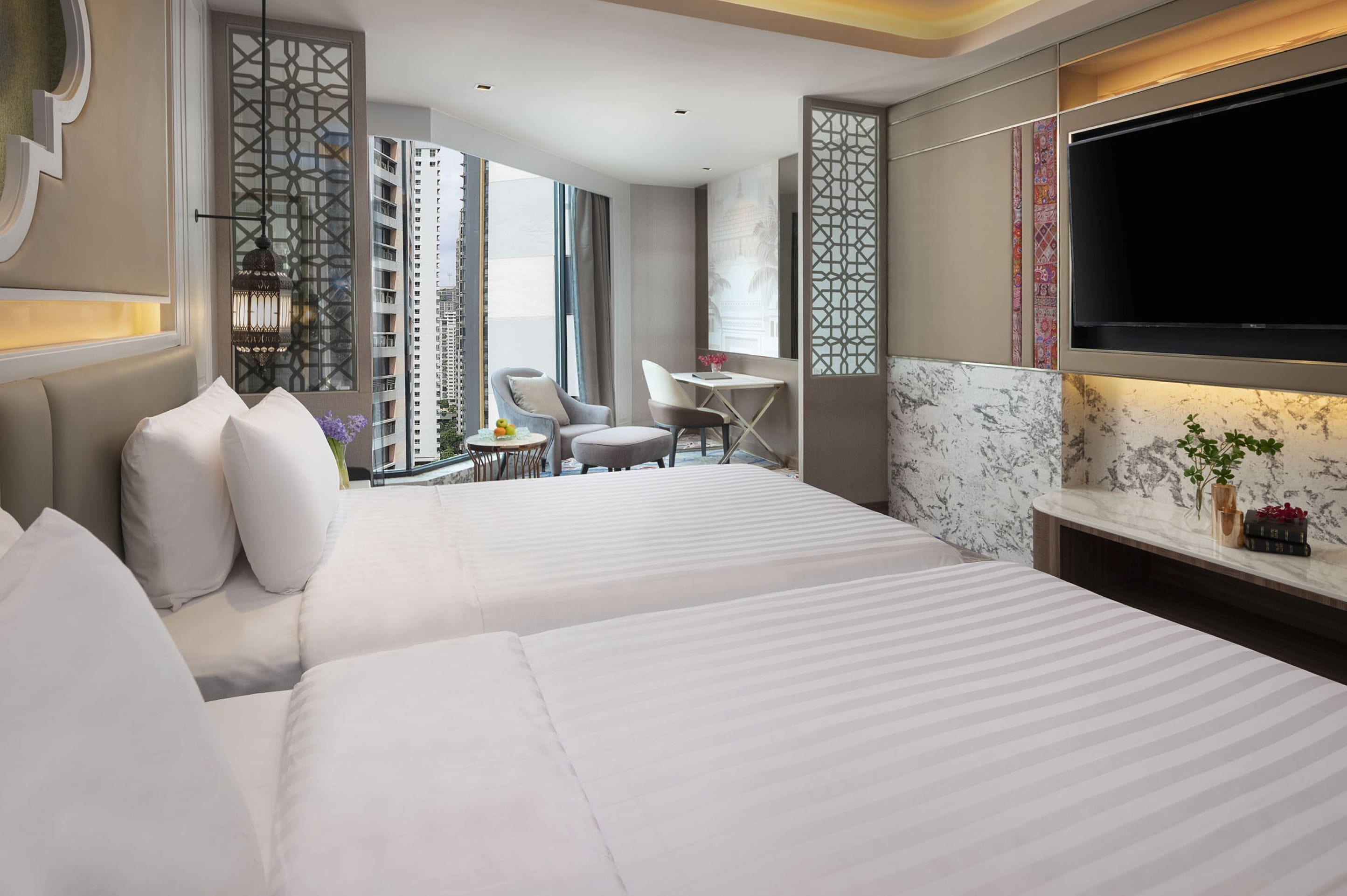 Quarto de hotel com duas camas, televisão, mesa pequena com cadeiras e vista para a cidade.