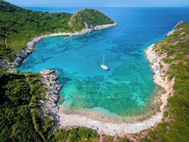 Paisagem costeira com mar azul límpido, costas rochosas e um veleiro.