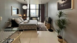 Quarto moderno com cama, mesa de cabeceira, abajur e uma grande janela com vista para a cidade.