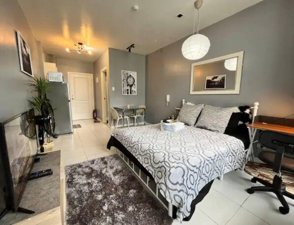 Quarto com cama, mesa de cabeceira, cadeira, escrivaninha e luminária pendente.