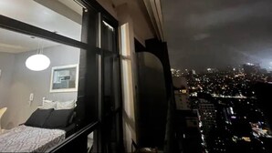 Quarto com cama, mesa de cabeceira e janela com vista para a cidade à noite.