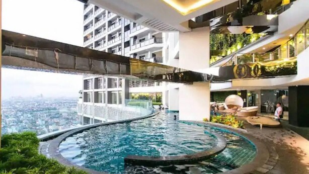 Piscina infinita no terraço com vista para a cidade, rodeada por vegetação e arquitetura moderna.