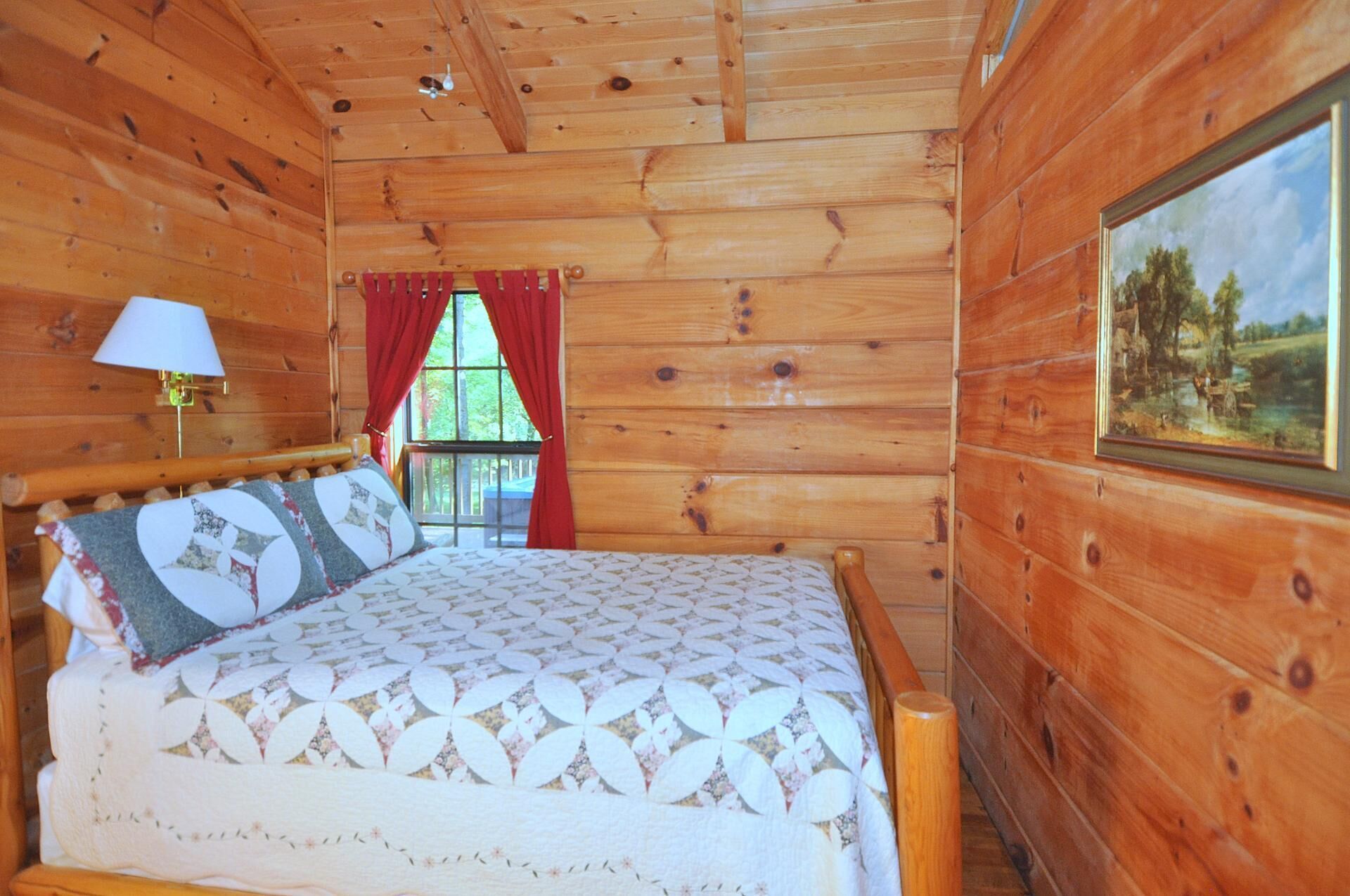 Quarto de cabana de madeira com cama, janela com cortinas vermelhas e um quadro na parede.