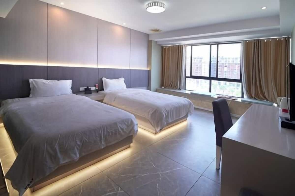 Quarto de hotel com duas camas, uma mesa de trabalho e uma janela grande com cortinas.