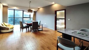 Quarto de hotel moderno com uma janela grande, área de jantar com mesa e cadeiras, e um espaço de estar acolhedor com um sofá.