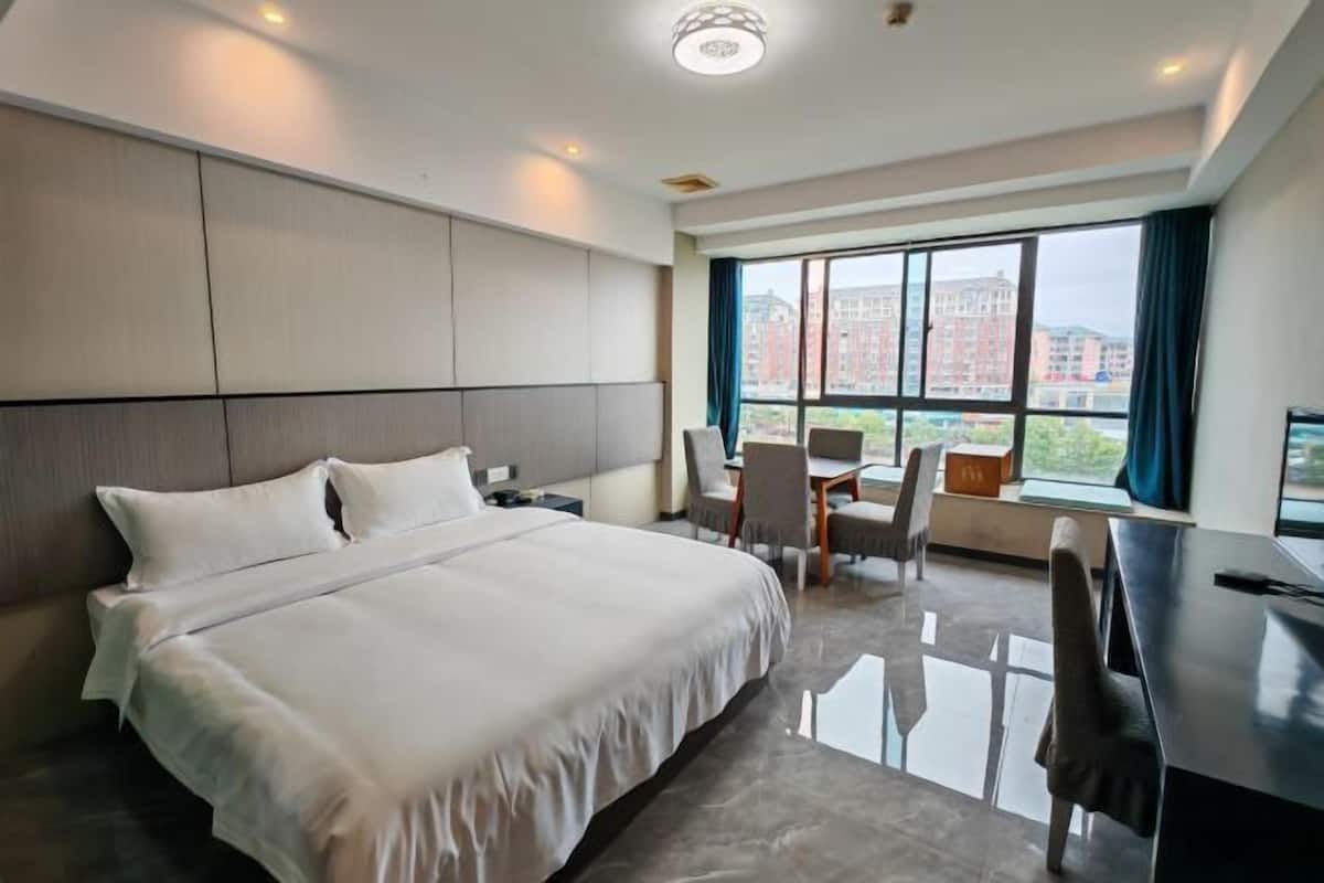 Quarto de hotel com uma cama grande, uma escrivaninha e vista para edifícios pela janela.