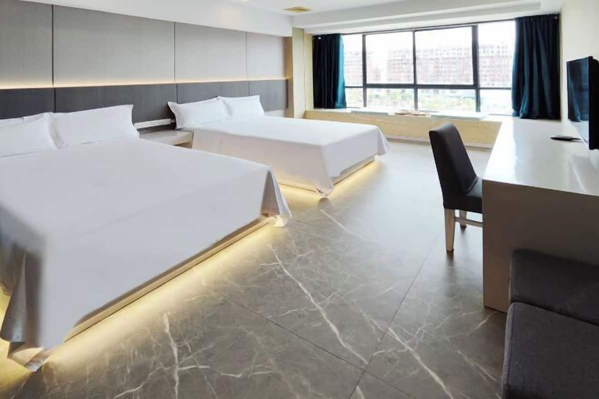 Quarto de hotel com duas camas, uma escrivaninha e uma cadeira.