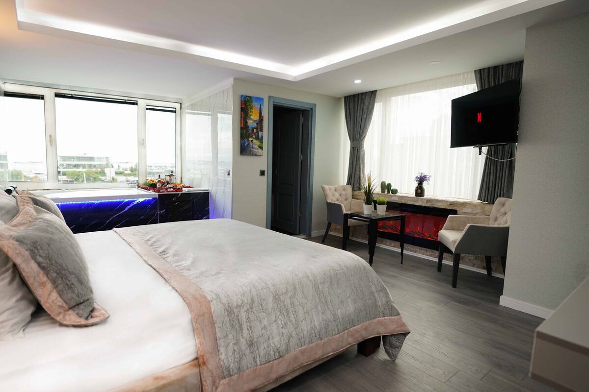Quarto de hotel moderno com uma cama grande, uma escrivaninha com cadeira, televisão de tela plana e lareira.