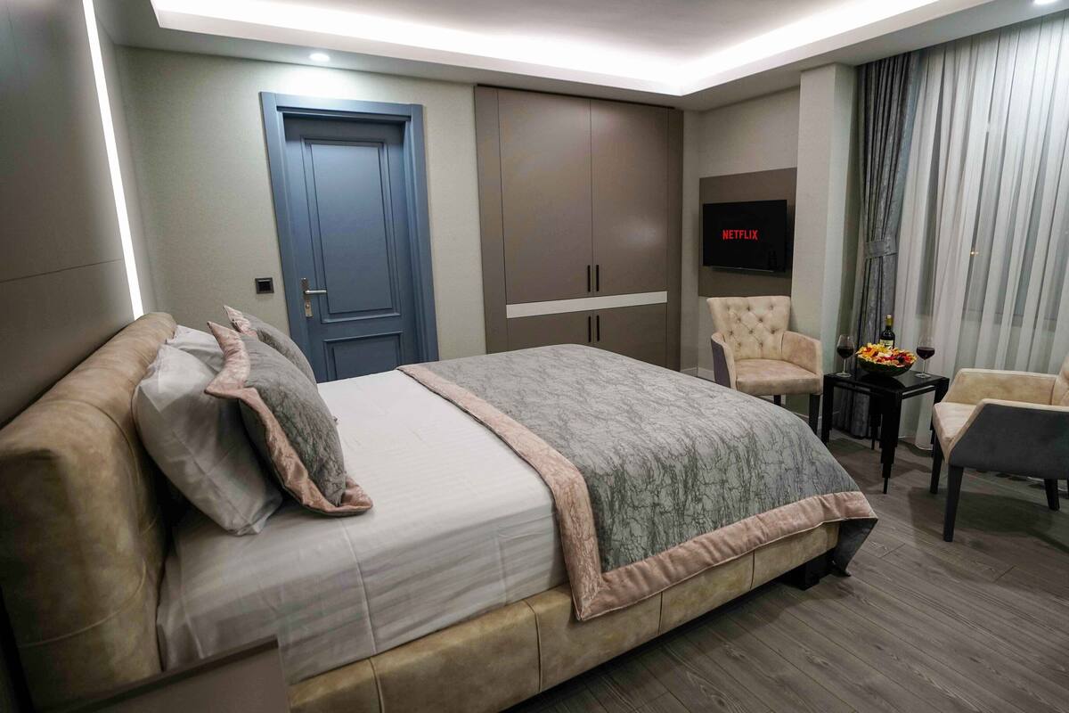 Quarto de hotel com cama, televisão, área de estar com mesa e porta.