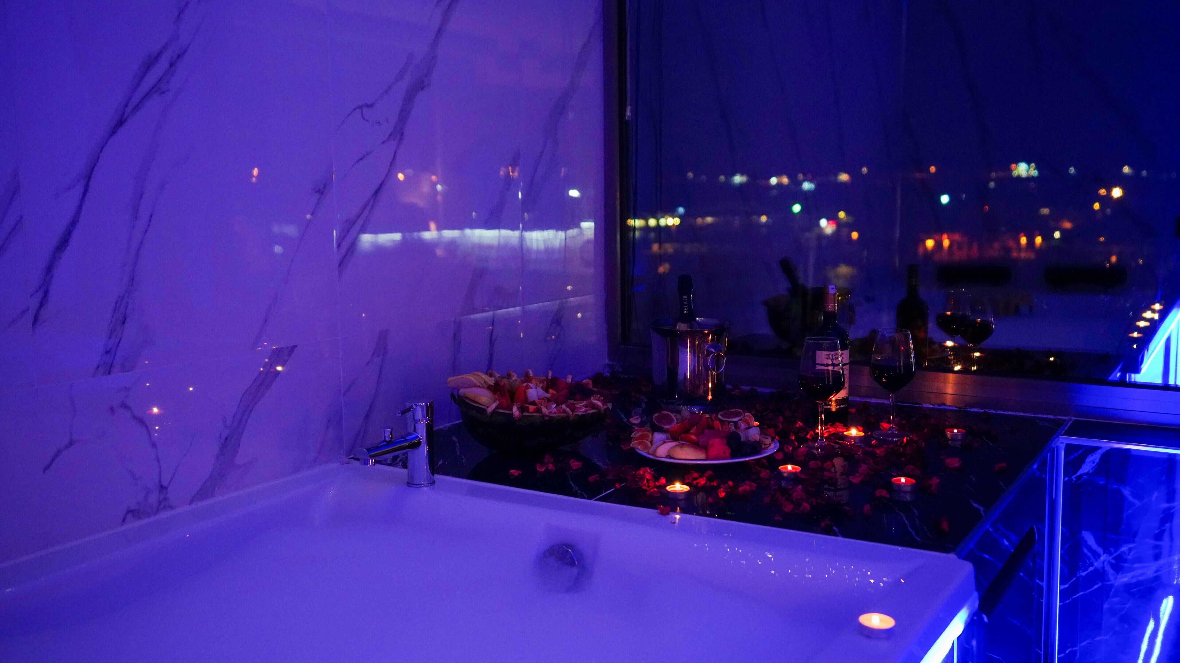 Casa de banho com lavatório de mármore, uma cesta de fruta, velas e garrafas de vinho.