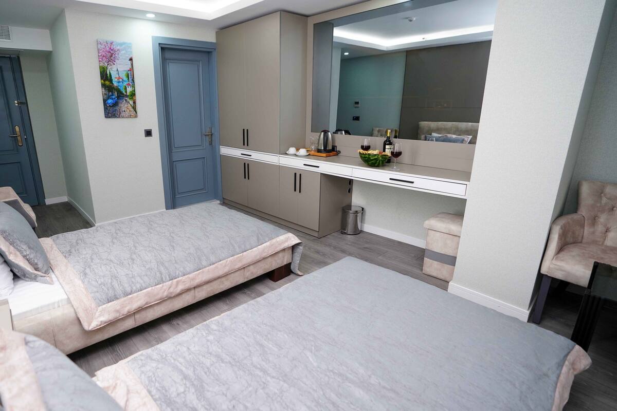 Quarto moderno com duas camas, um guarda-roupa grande, uma toucador com espelho e um pequeno espaço de estar.