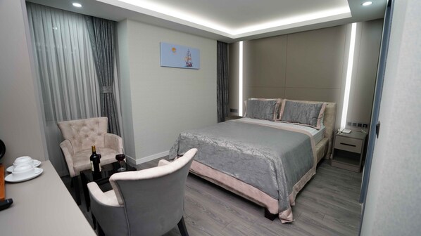 Quarto de hotel moderno com cama, uma cadeira, mesa de cabeceira com garrafa e copo, e um quadro na parede.